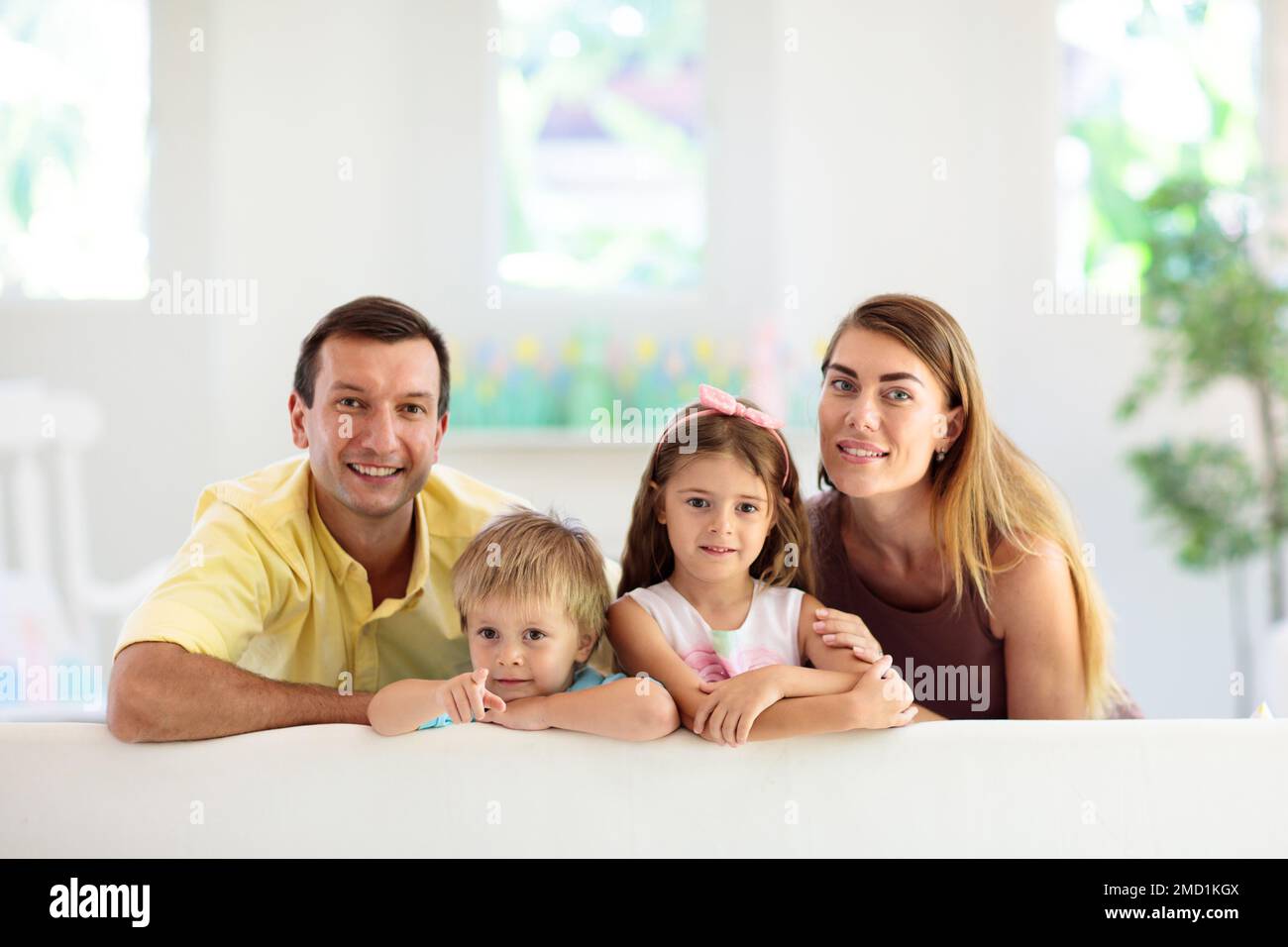 Happy family at home. Parents and kids sitting on white couch in sunny ...