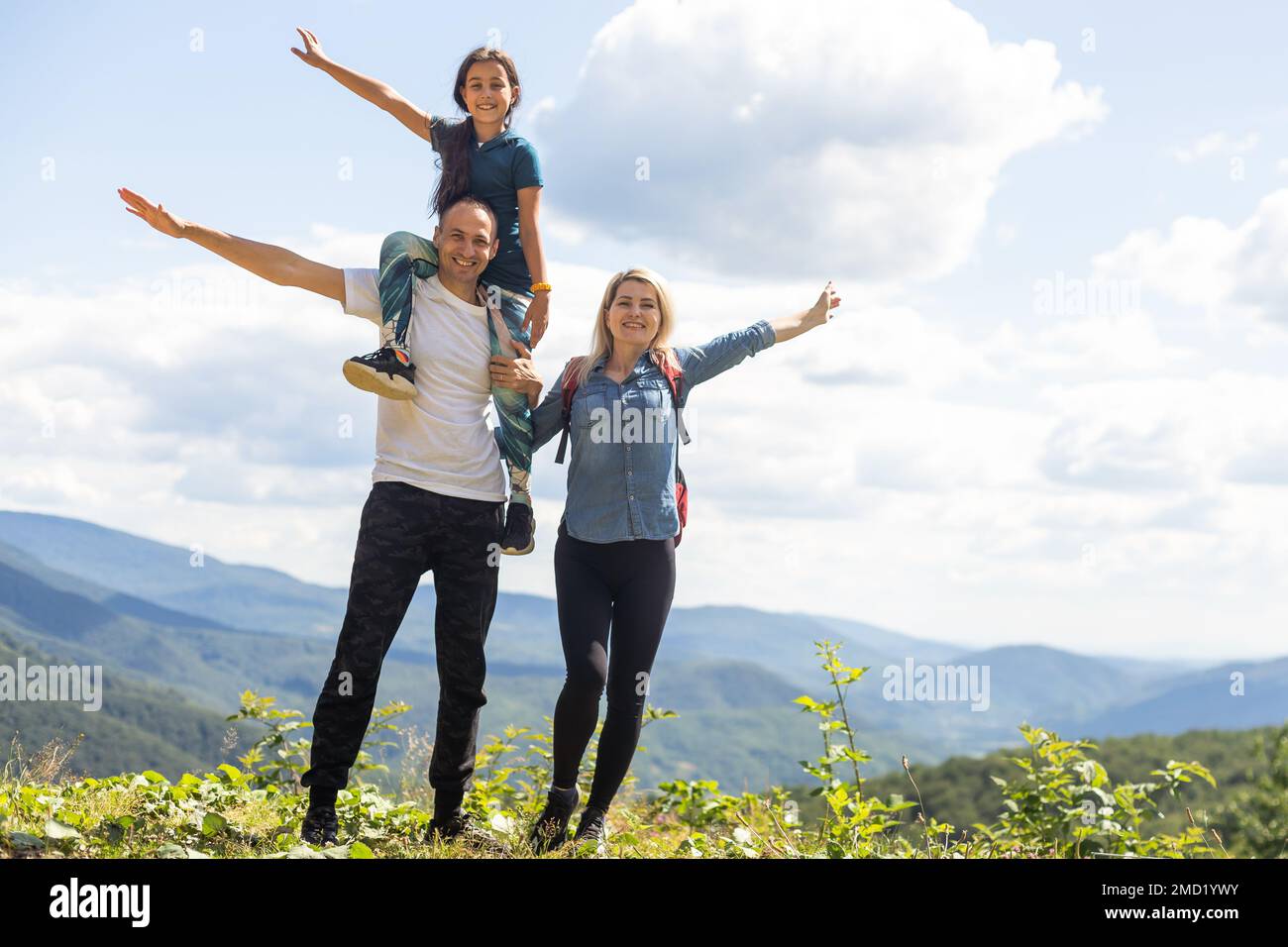 Mother, father hugging son, and daughter in summer mountains. Happy family smiling and standing ...