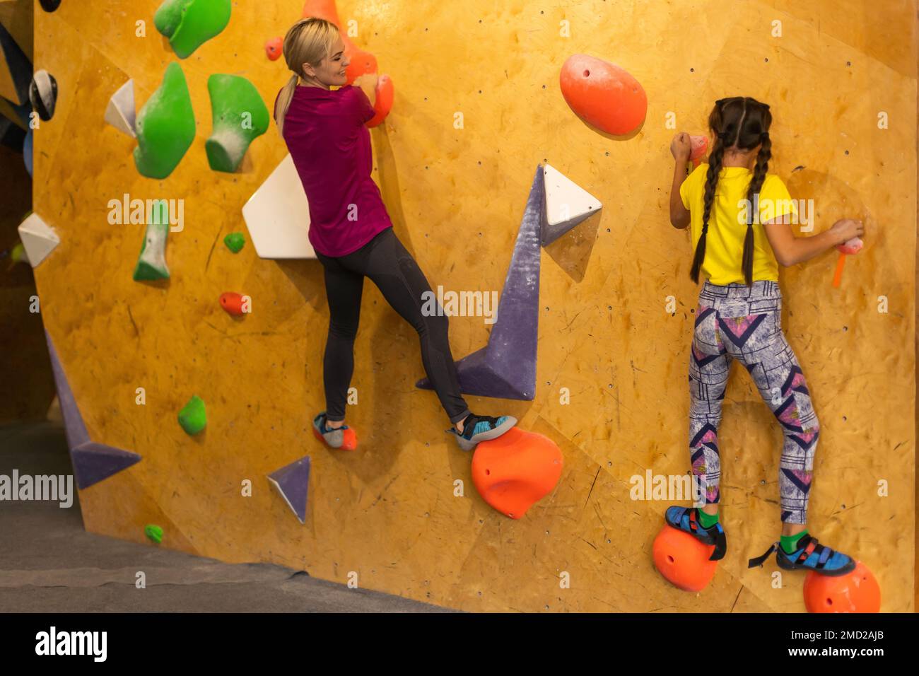 Young female bouldering instructor helping boy climb artificial wall ...