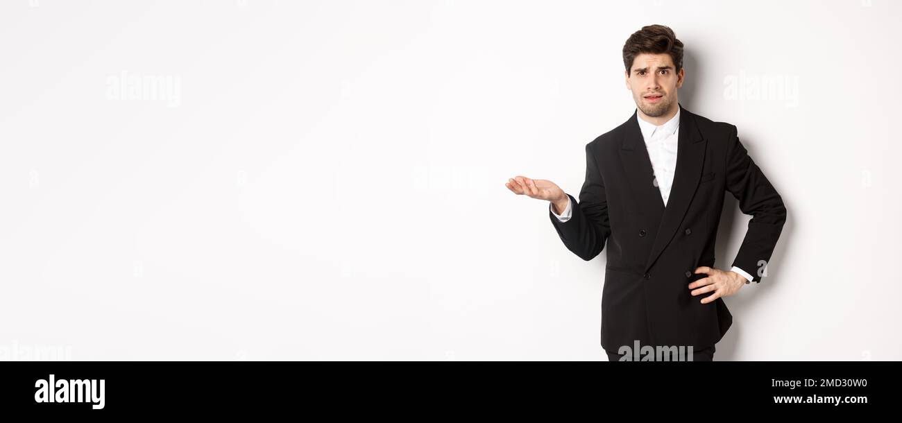 Image of confused handsome man in formal suit, raising hand and ...
