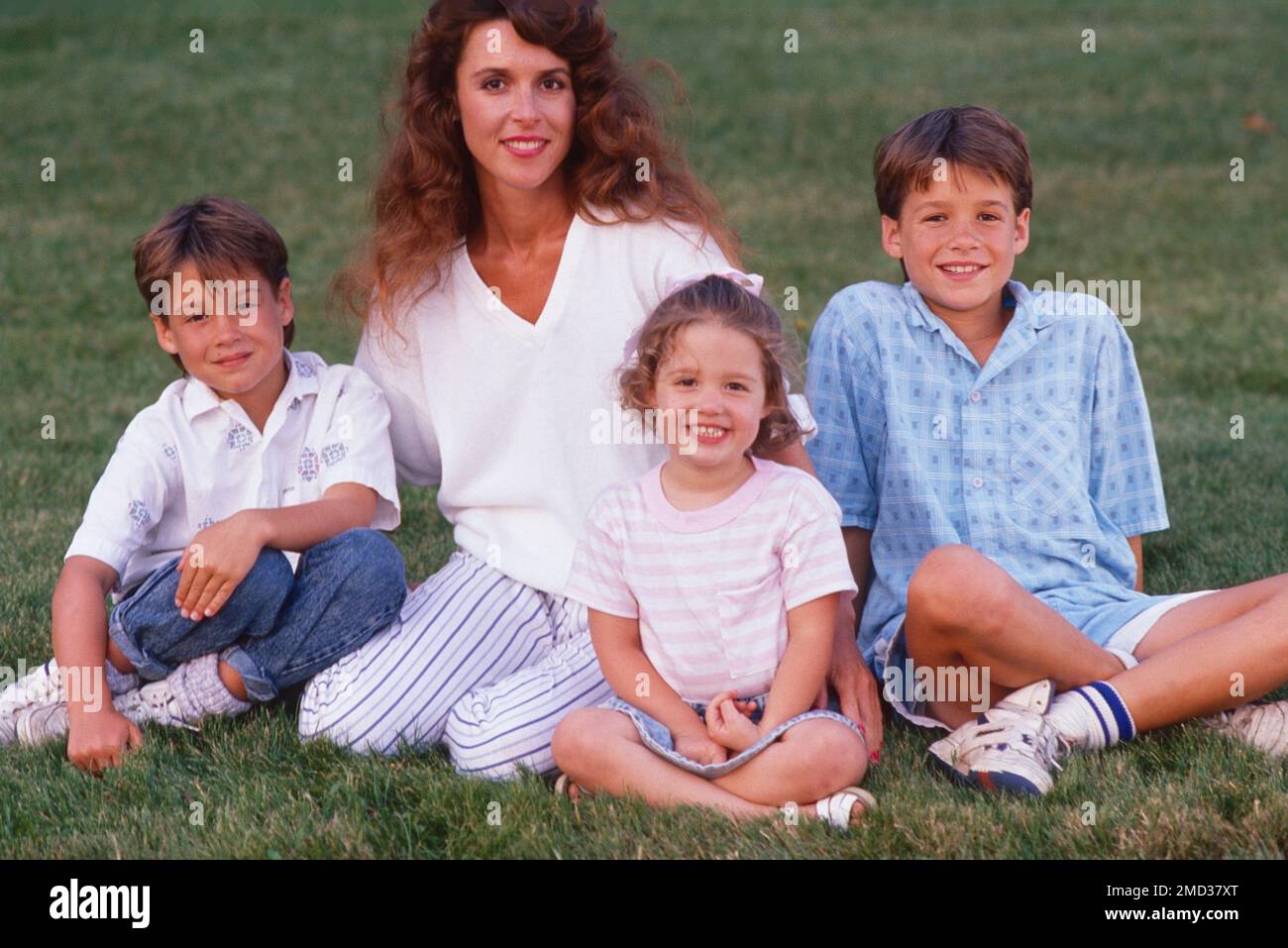 Young mother of three, sitting outside on the grass, posing for a ...