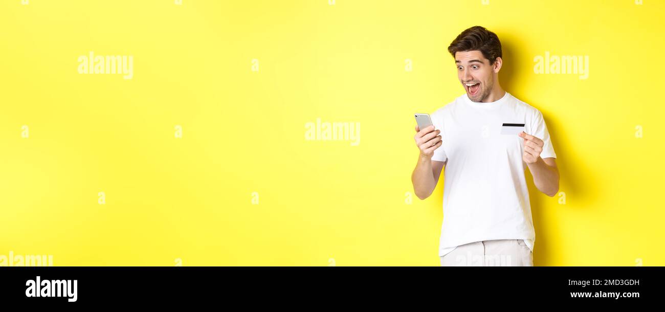 Man looking surprised at smartphone, shopping online, holding credit ...