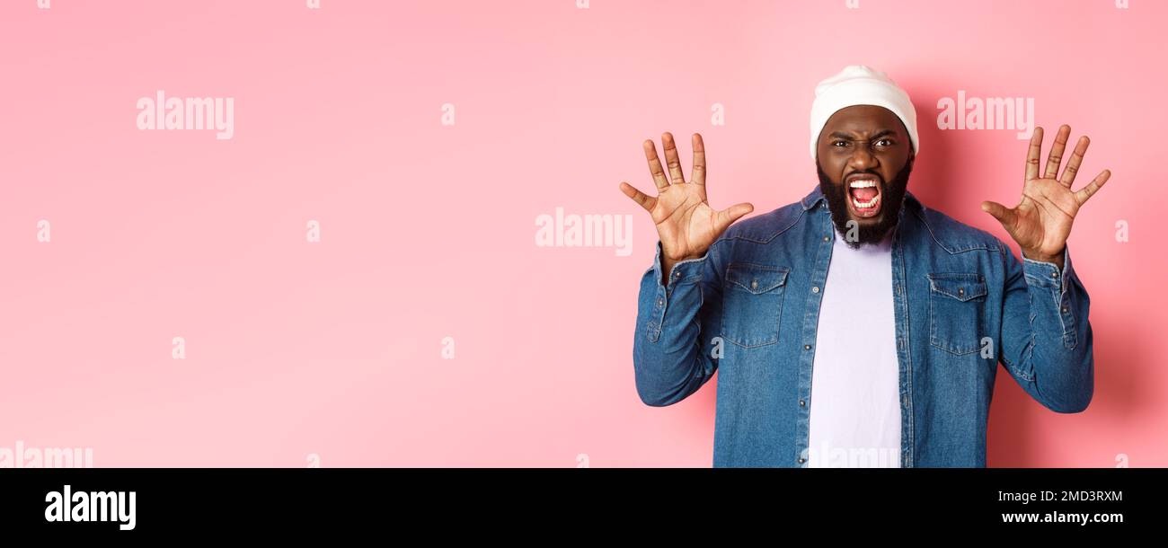 Angry african-american guy in beanie, scare you, roaring and screaming ...