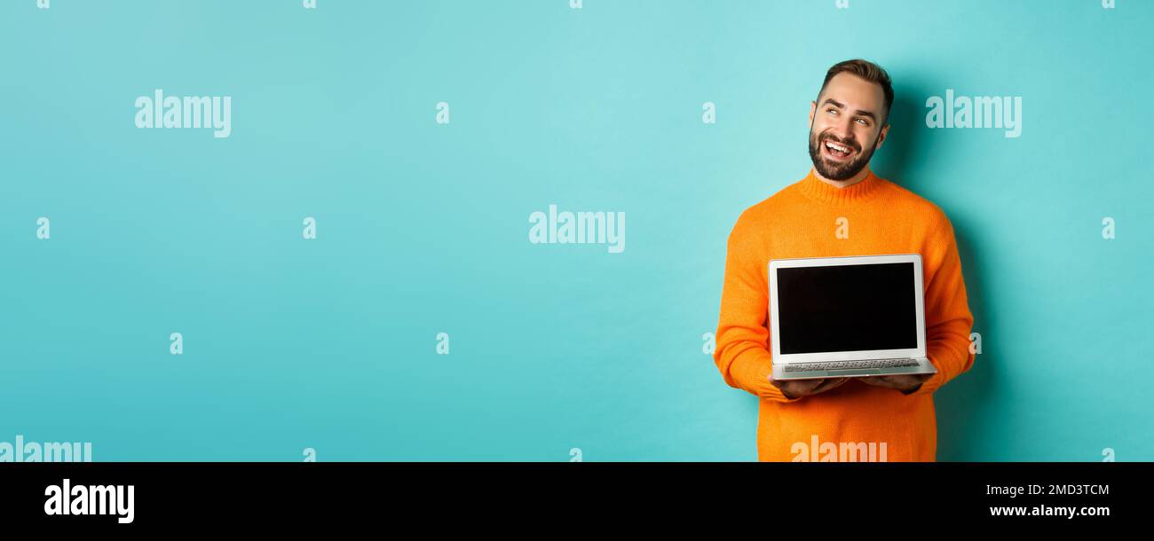 Happy caucasian man thinking and showing laptop screen, smiling pleased ...