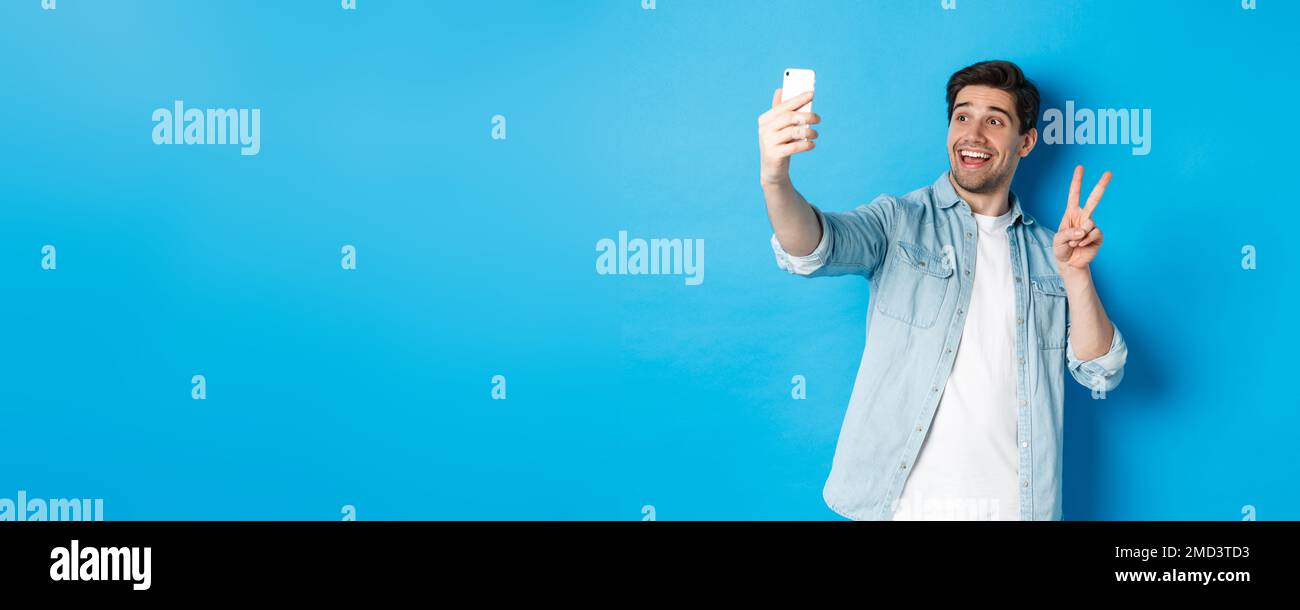 Happy man taking selfie and showing peace sign on blue background ...