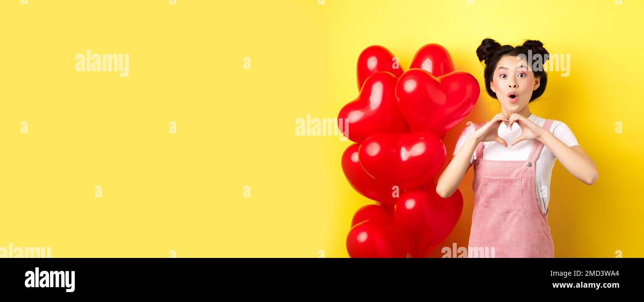 Surprised asian woman looking in awe, showing heart gesture, making ...