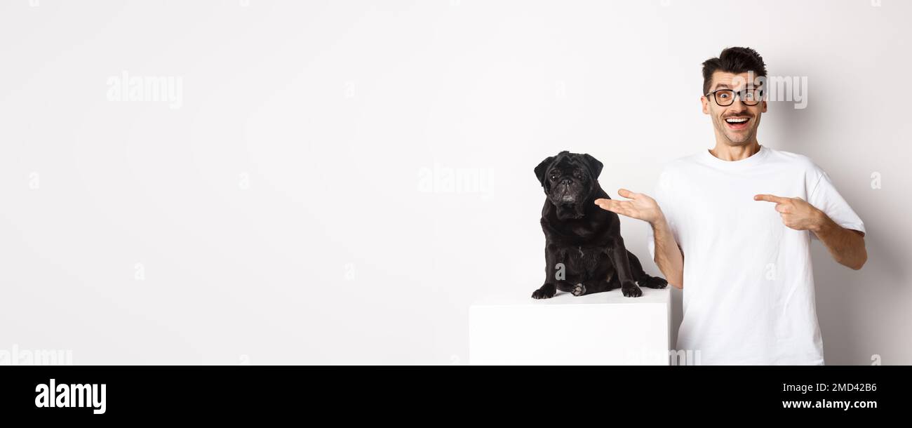 Cheerful young man pointing finger at his dog, showing small cute black ...