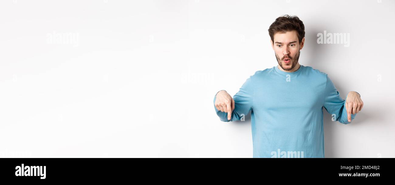 Handsome man pointing down with impressed and happy face, smiling and ...