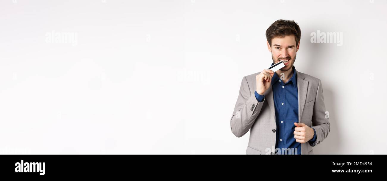 Successful young businessman in suit biting his credit card and looking ...