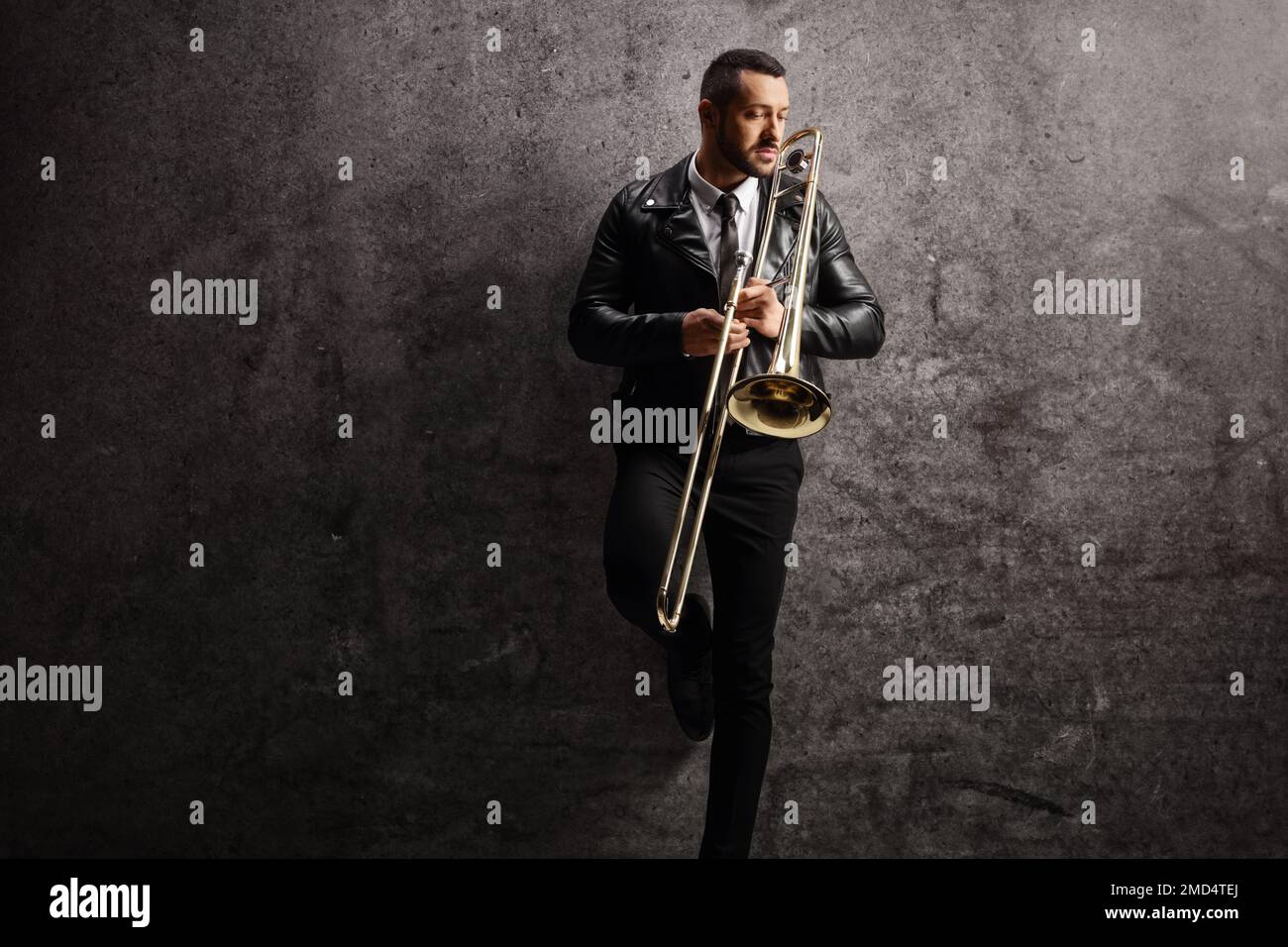Young man holding a trombone and standing against a gray wall Stock ...