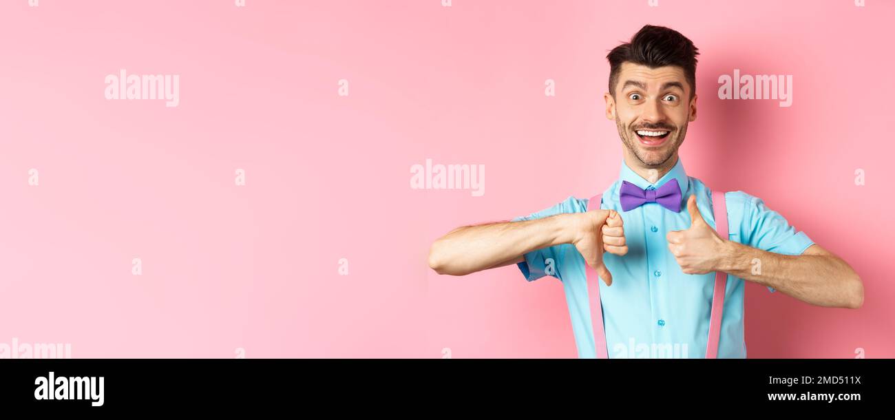 Funny young man smiling and showing thumbs up down, judging something ...
