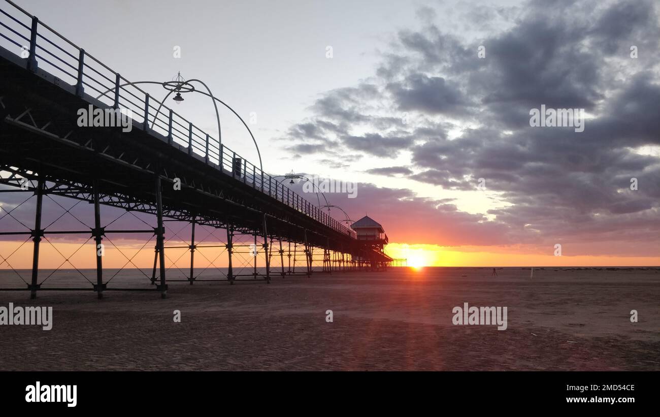 A beautiful sunset scene at a beach with a pier and a lifeguard tower ...