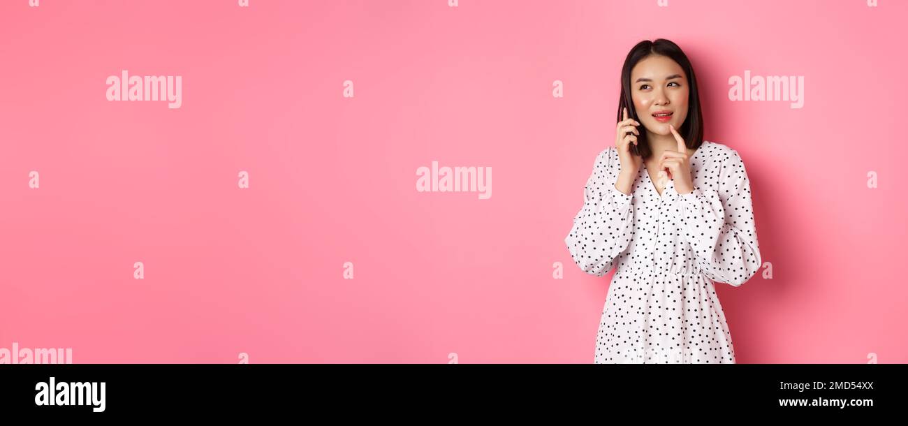 Thoughtful asian woman calling on mobile phone to make order, thinking ...