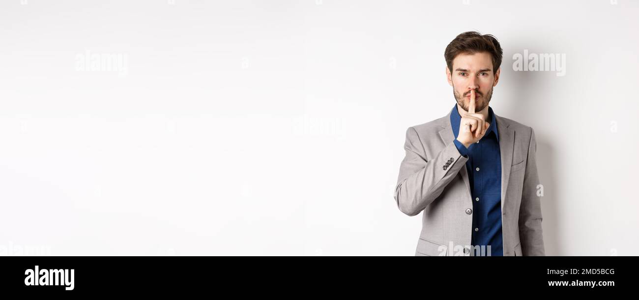 Handsome macho man in suit shushing at camera, press finger to lips ...