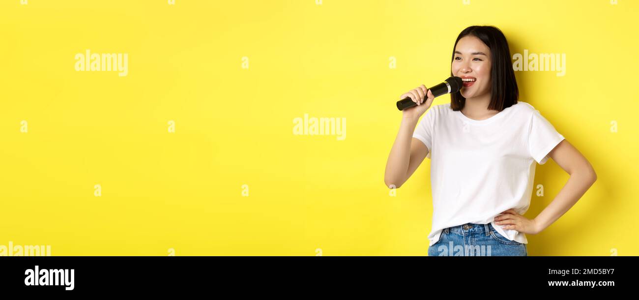 Happy asian woman singing song in karaoke, holding microphone and ...