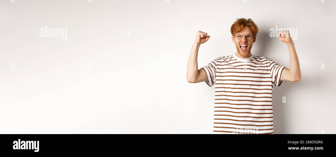 Joyful redhead guy raising hands up like winner, winning prize and ...