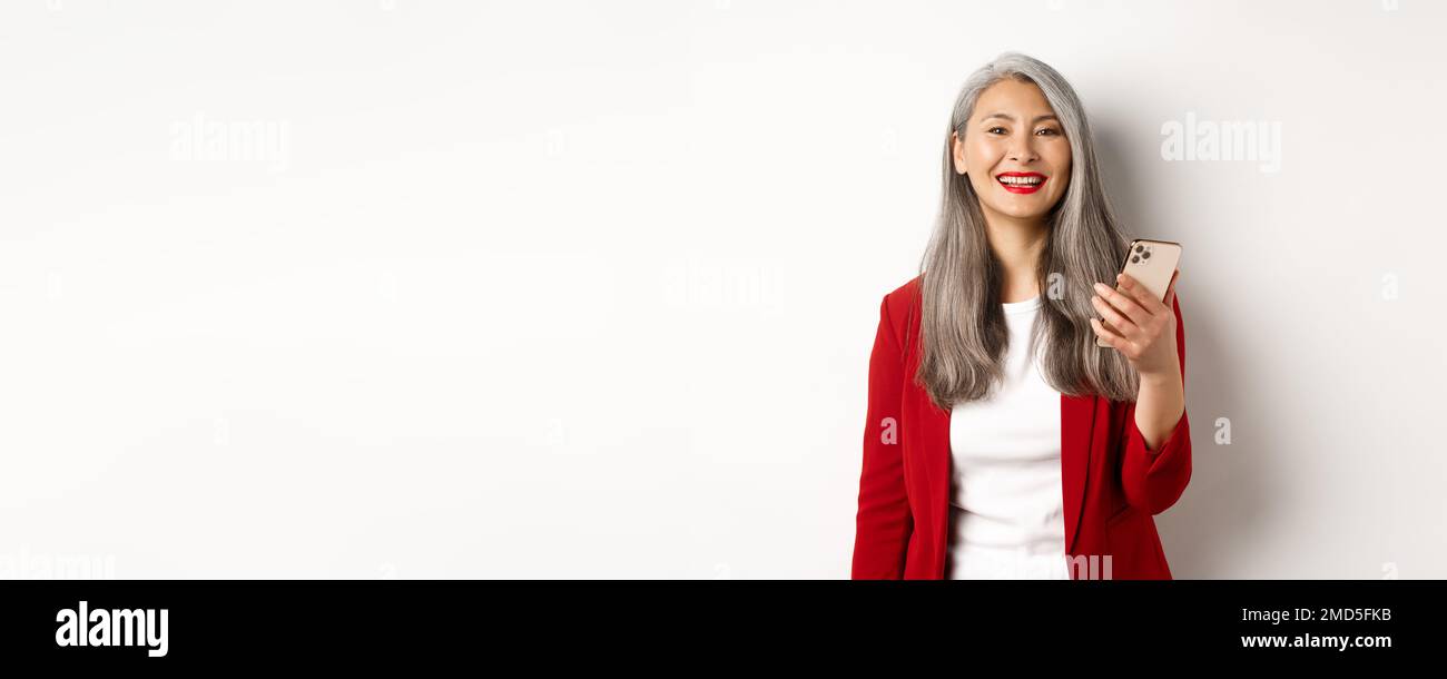 Asian female entrepreneur in red blazer using smartphone, smiling happy ...