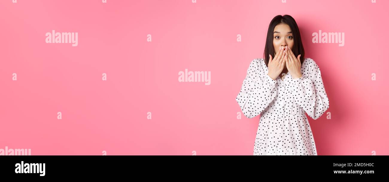 Worried asian girl in dress looking concerned, cover mouth and gasping ...