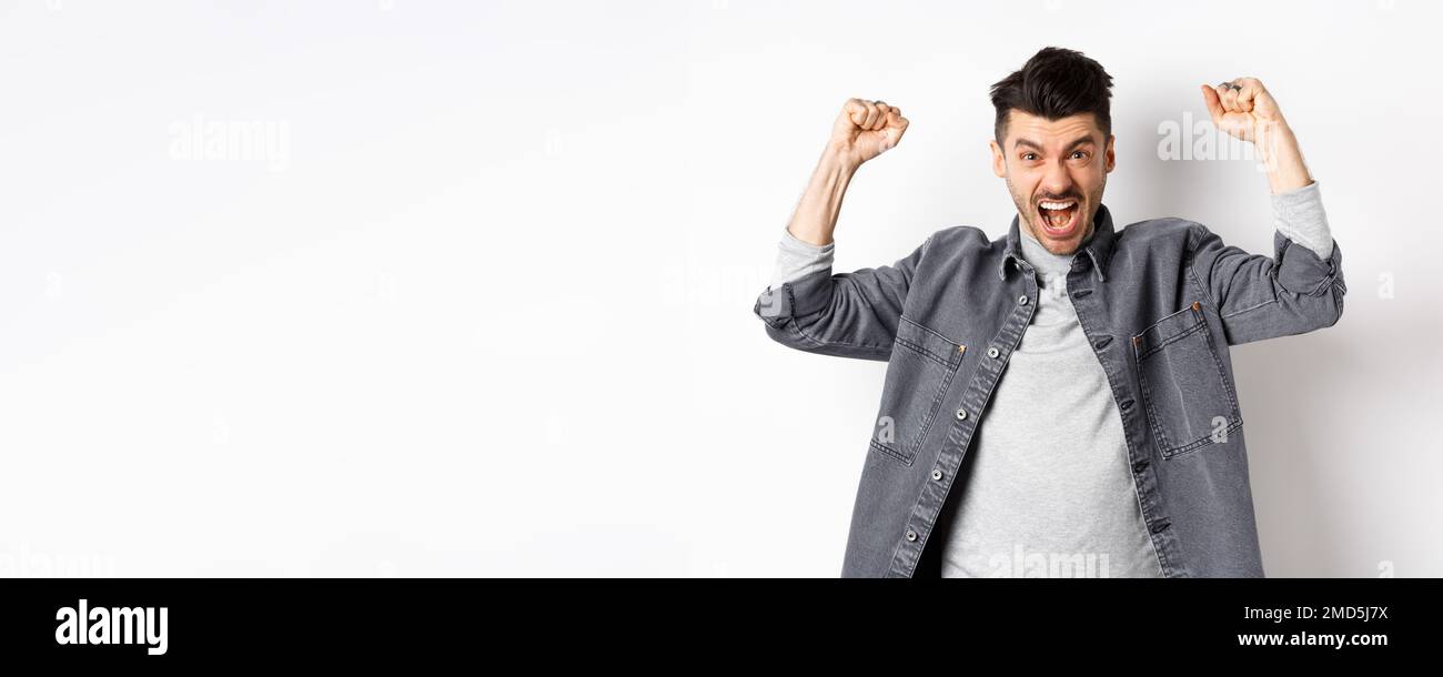 Motivated young man shouting and raising hands up, watching sports game ...