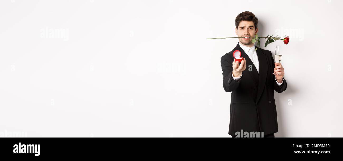 Romantic young man in suit making a proposal, holding rose in teeth and ...