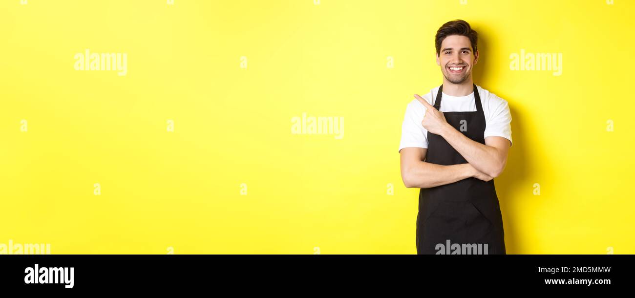 Happy barista pointing finger left and smiling, wearing black apron ...