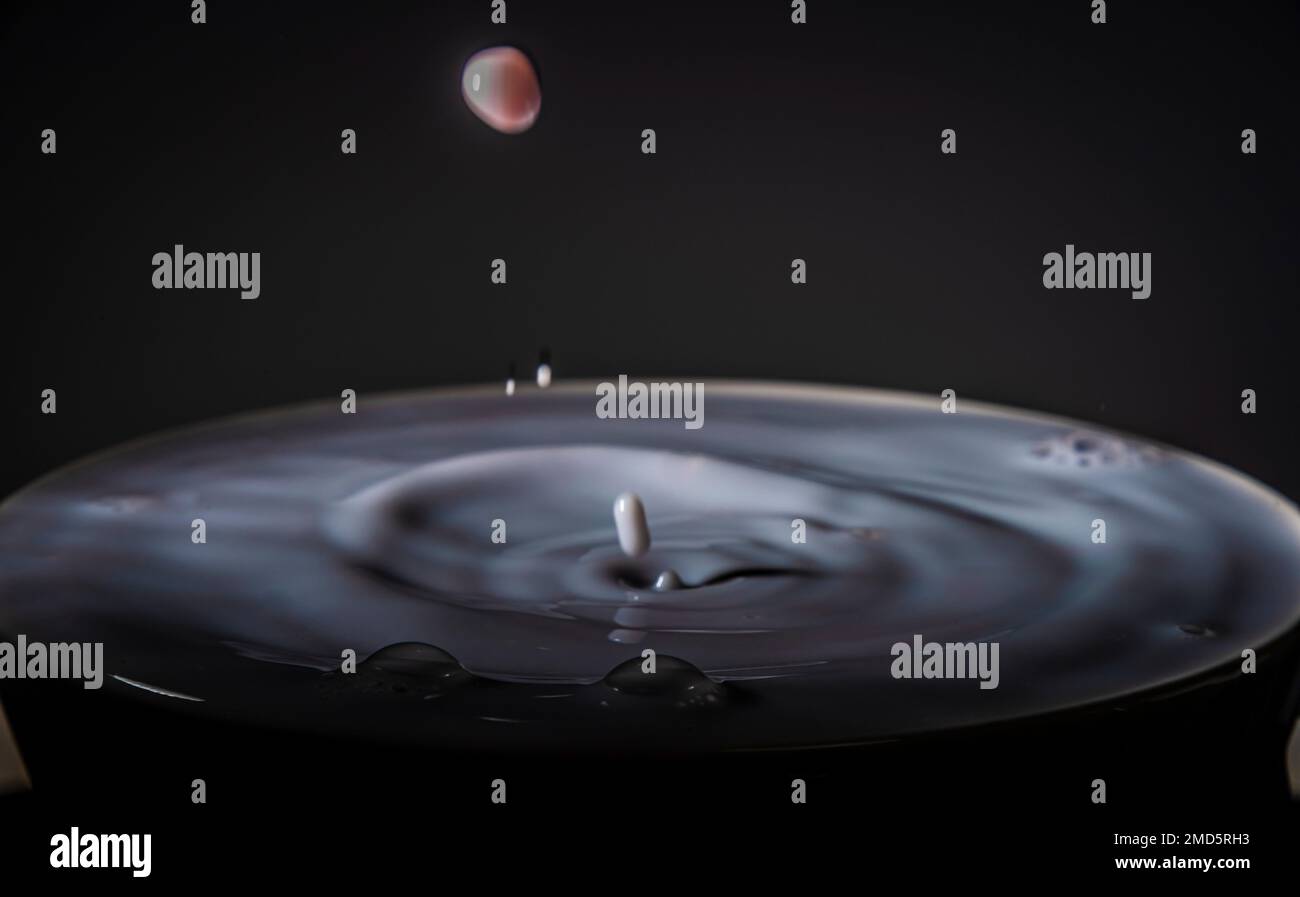 Color fresh sweet milk drops into another color of milk in cup with ...