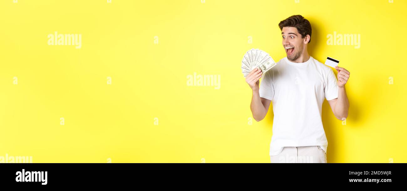 Cheerful guy looking at money, holding credit card, concept of bank ...