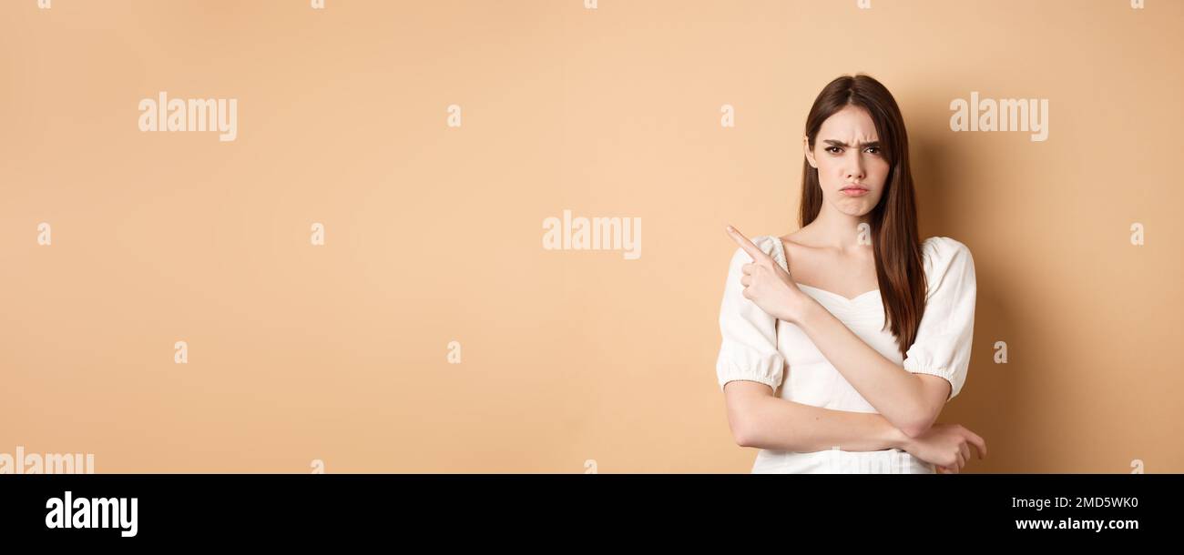Angry frowning girl pointing left at empty space, looking disappointed ...
