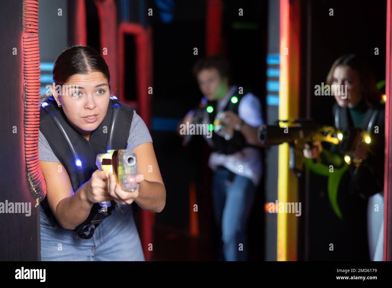 Joyous girl with laser pistol playing laser tag with friends on ...