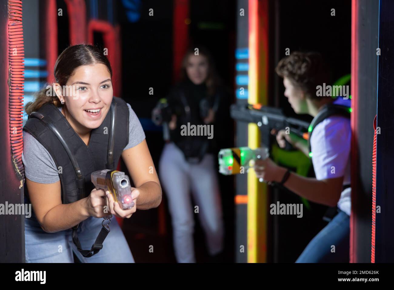 Positive girl holding laser pistol playing laser tag game with friends ...
