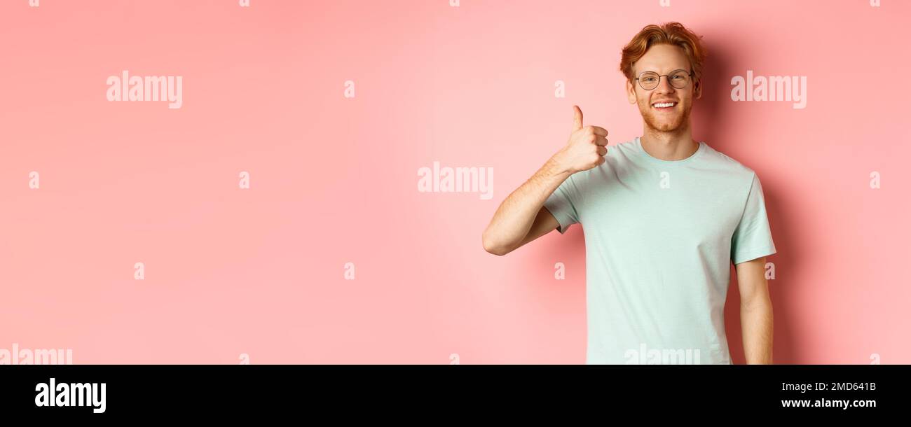 Cheerful redhead man in glasses and t-shirt, showing thumbs up with ...