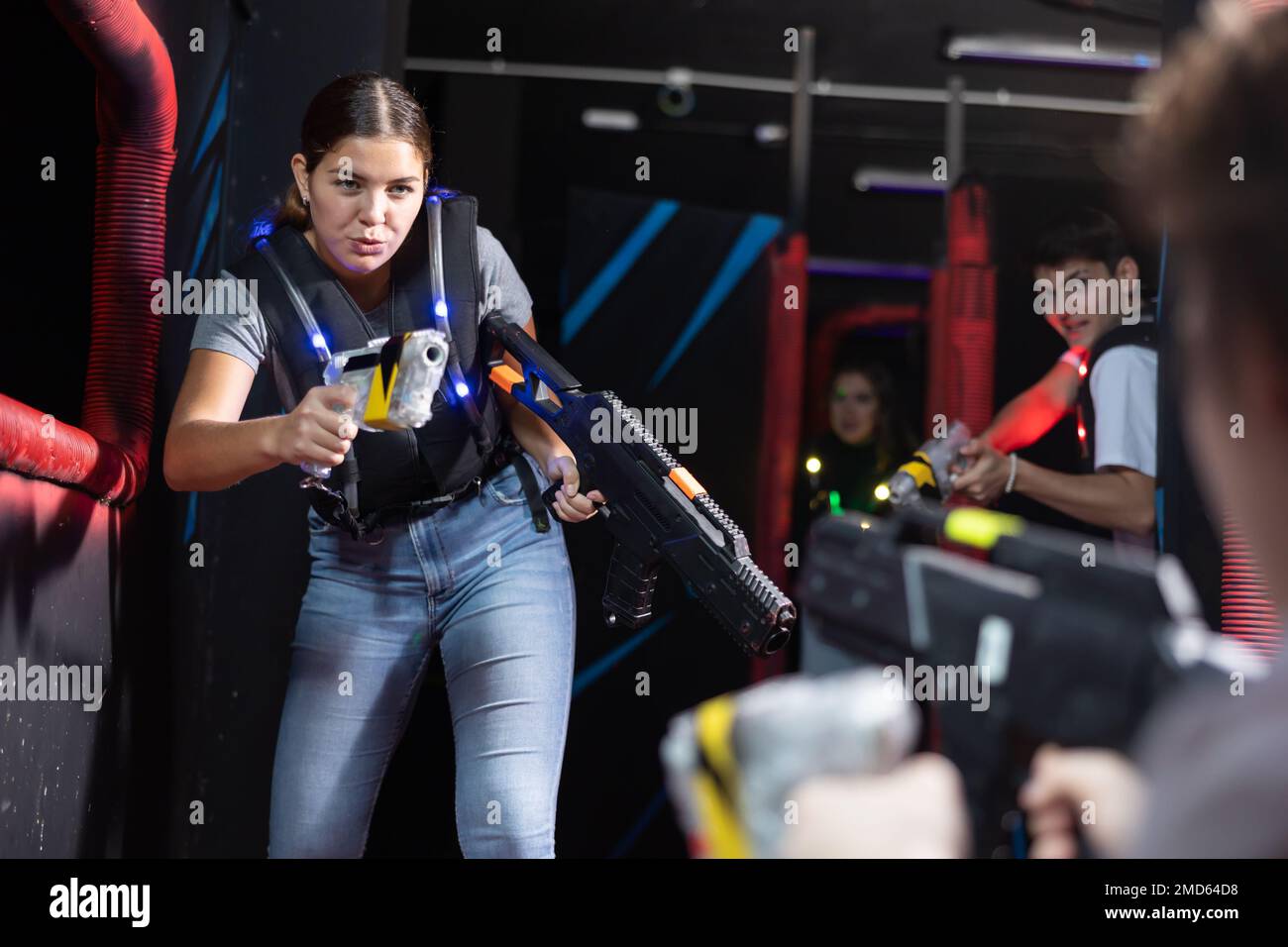 Joyous girl with laser pistol playing laser tag with friends on ...