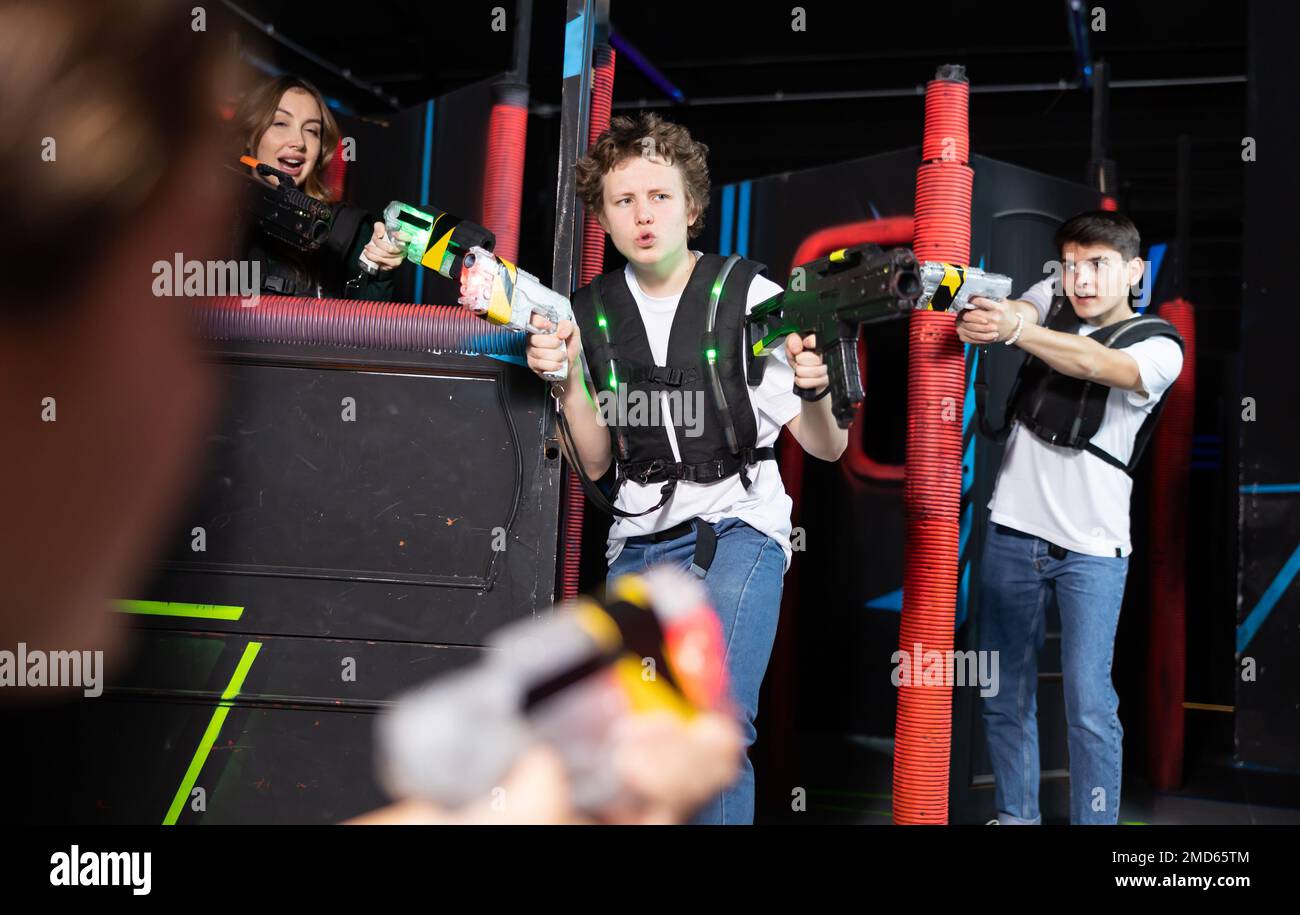 Laughing players mens and womens playing in teams in dark laser tag ...