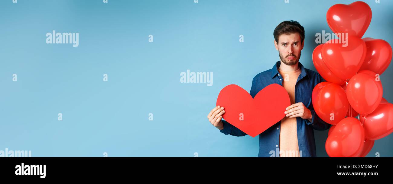 Sad man looking heartbroken and lonely, holding paper red heart and ...