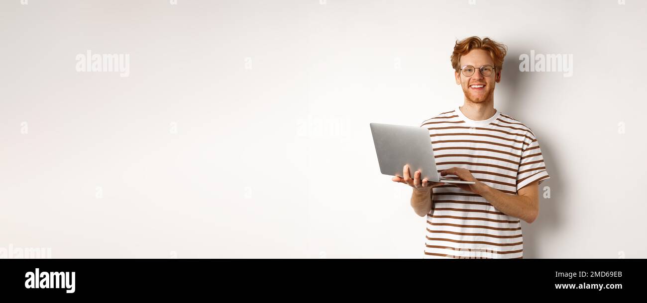 Smiling young man working on laptop and looking joyful, standing over ...