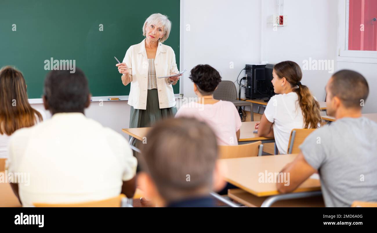 Elderly female teacher giving lecture to group of students in ...