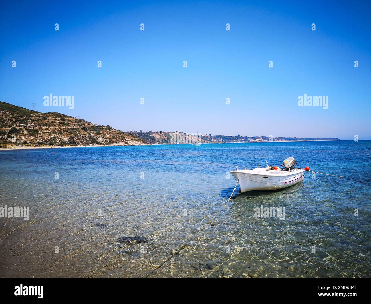 A boat parked in the crystal clear sea with a mountain in the ...