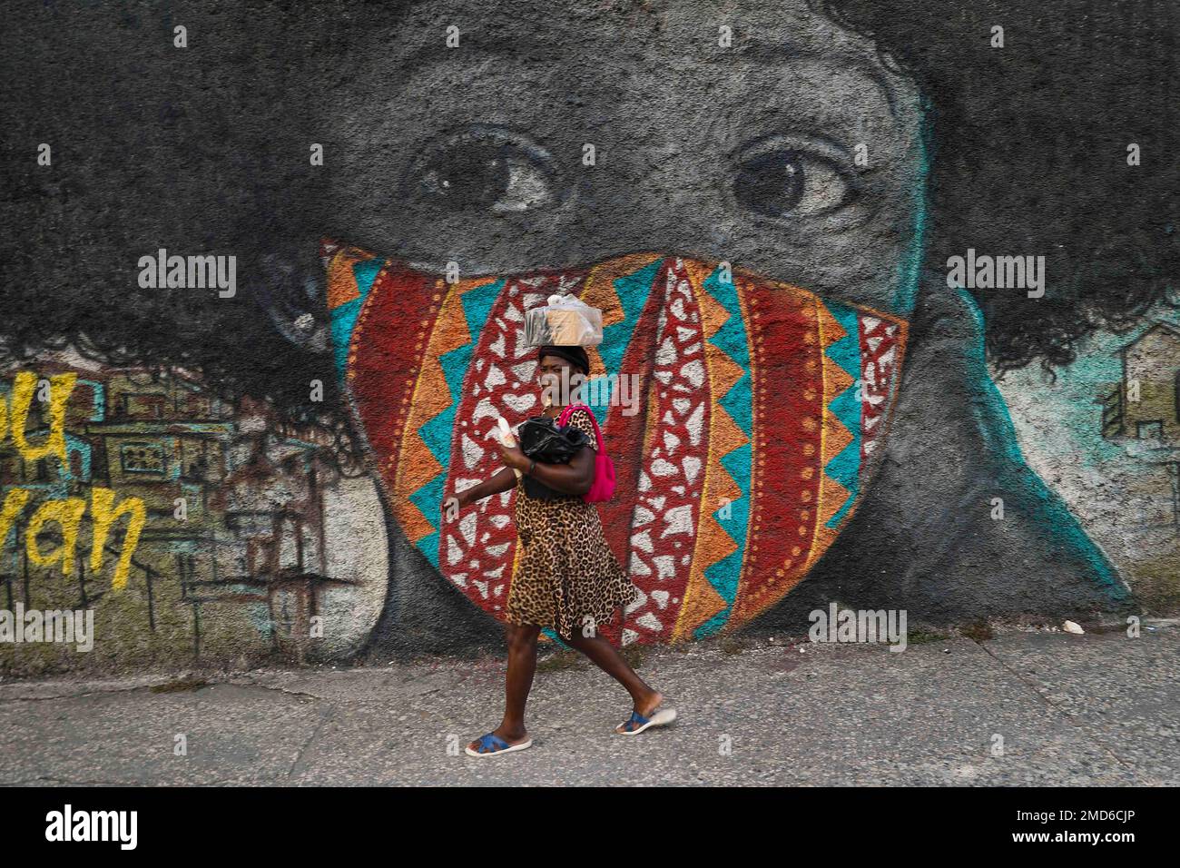 A woman walks past a mural of a woman wearing a protective face mask in ...