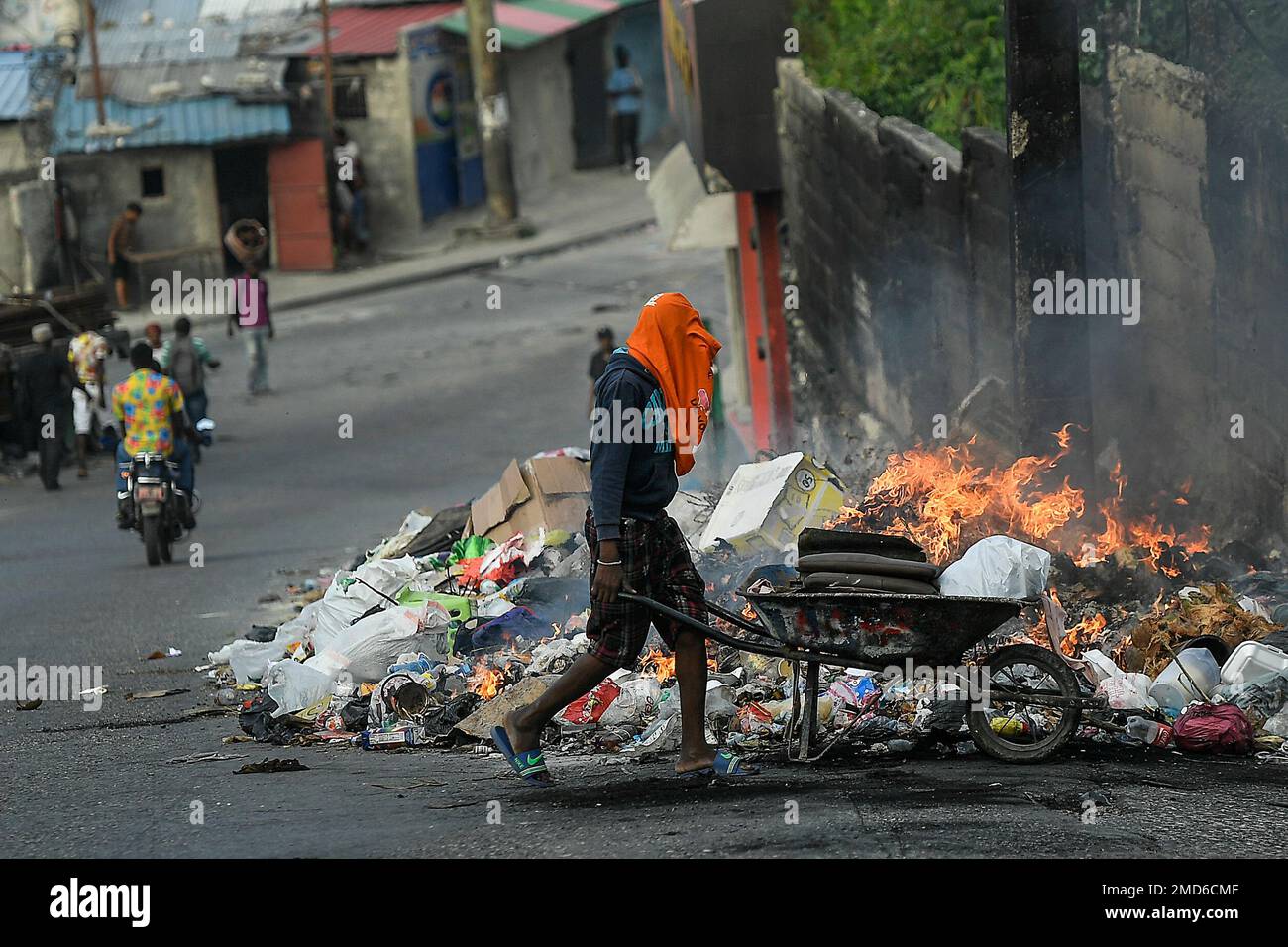 A youth pushes a wheelbarrow past a burning pile of garbage in Port-au ...