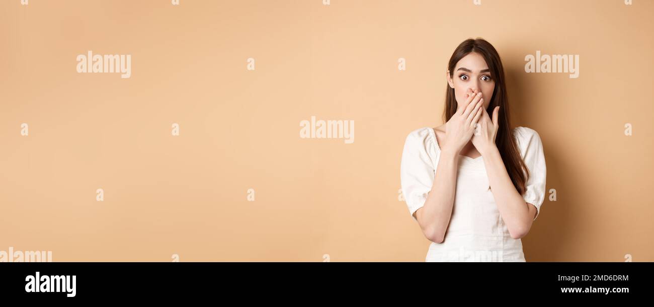 Shocked woman covering mouth with hands and staring startled at camera ...
