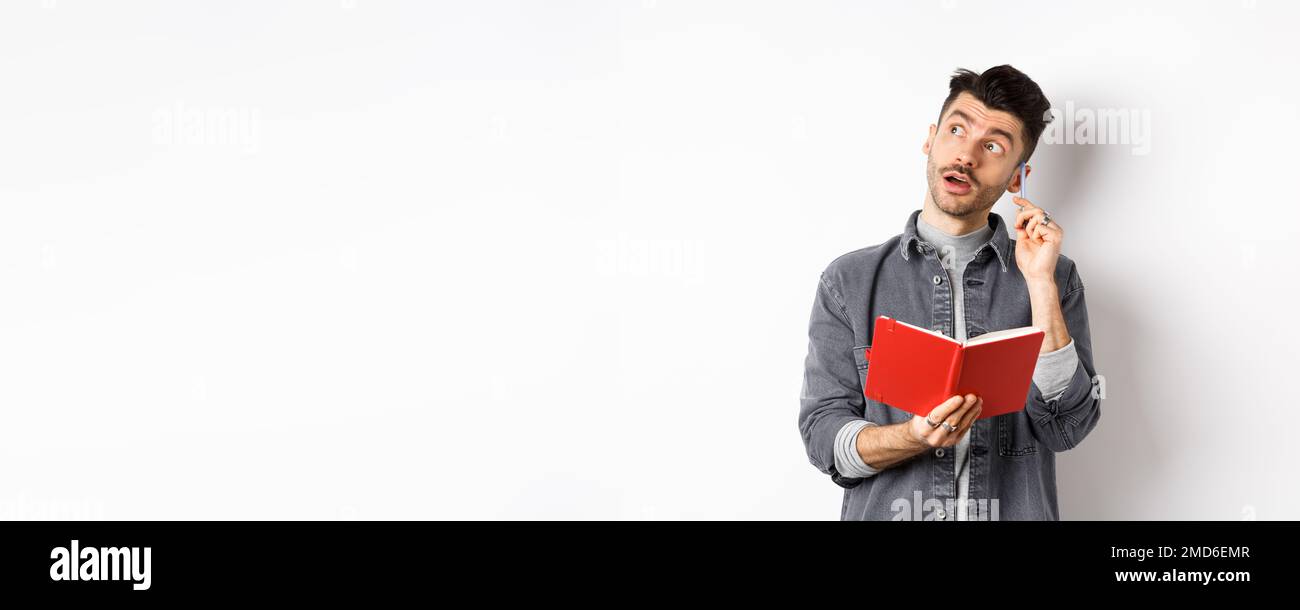 Image of pensive young man writing down ideas in planner, looking ...
