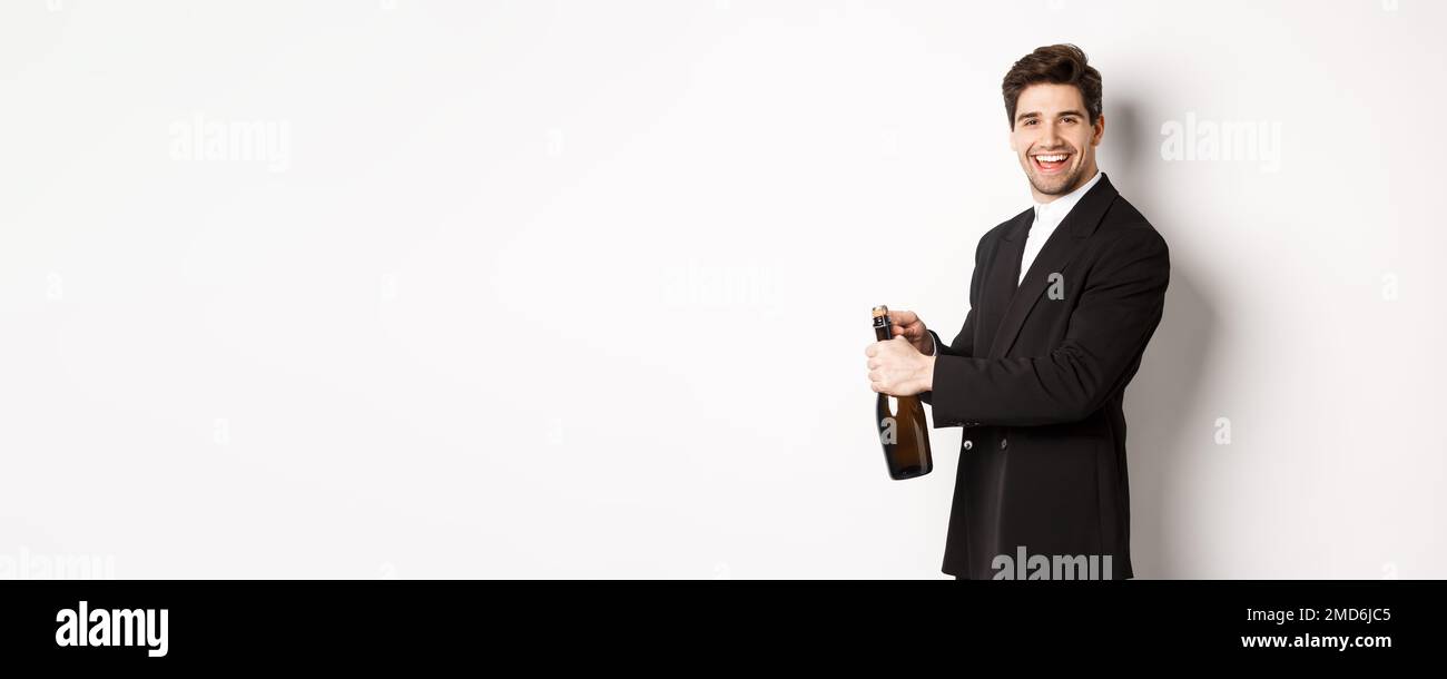 Handsome smiling man in trendy suit open a bottle of champagne ...