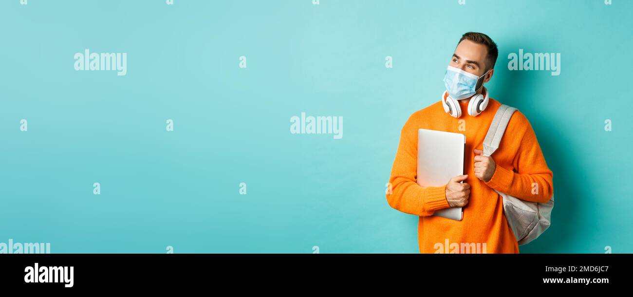 Handsome caucasian man with headphones and backpack, holding laptop and ...