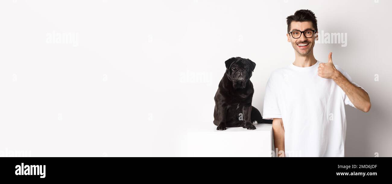 Image of dog owner and cute black pug looking at camera, man showing ...