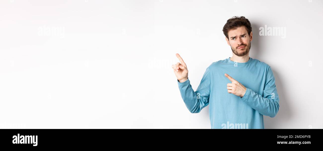 Skeptical and unimpressed young man grimacing, pointing fingers and ...
