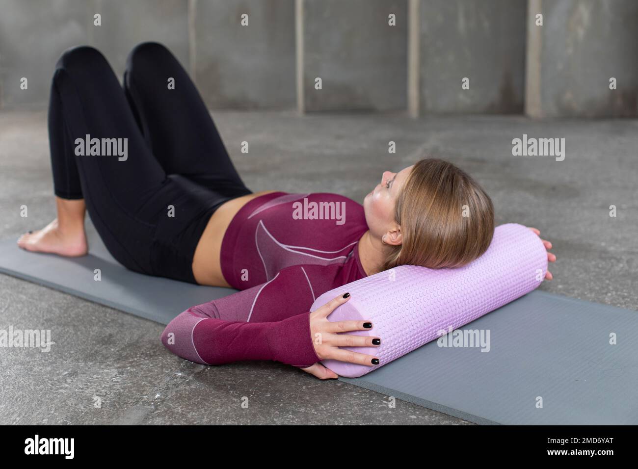 A young woman in sportswear performs a myofascial release, relaxes the ...