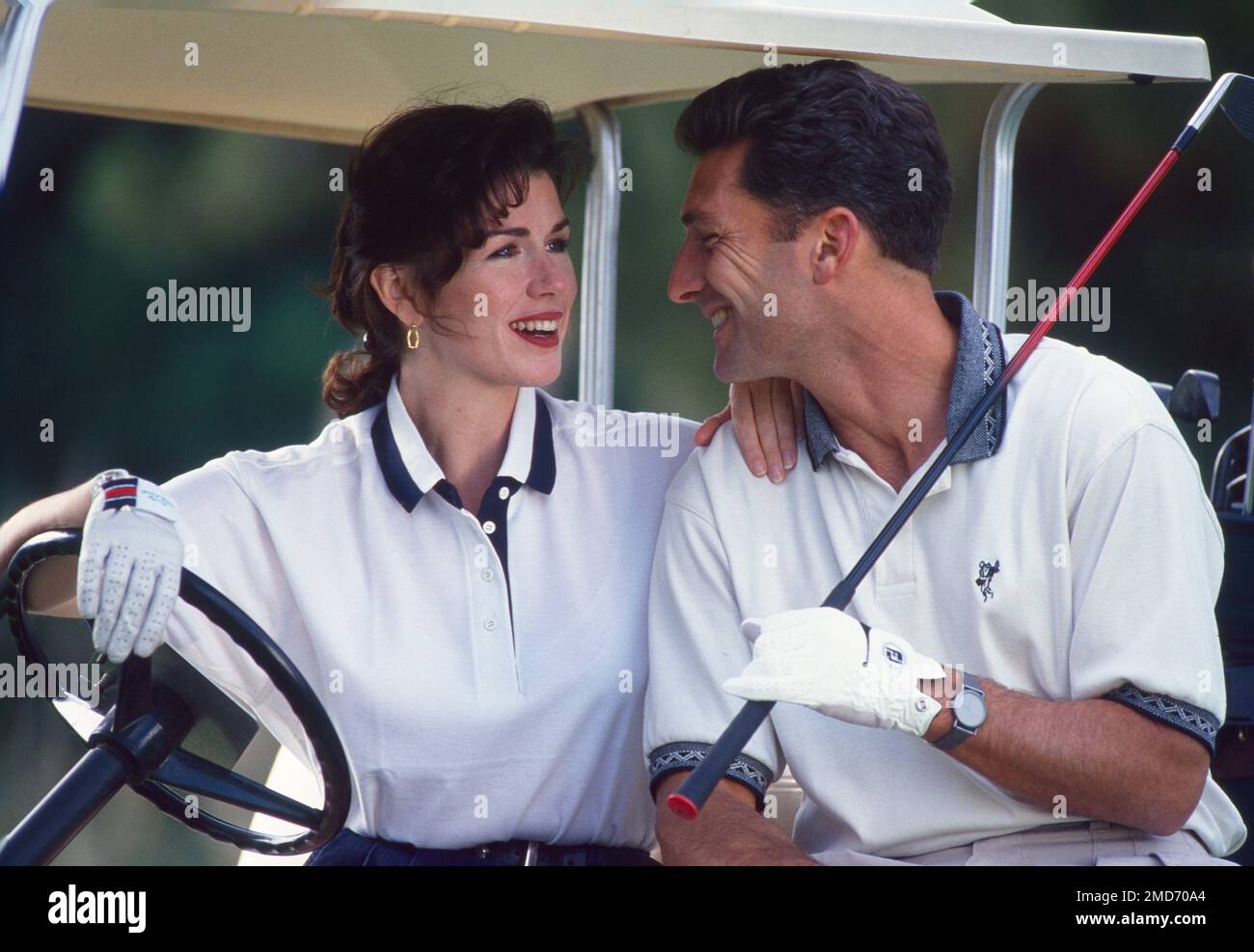 Young couple out golfing sitting in a golf cart laughing it up and ...