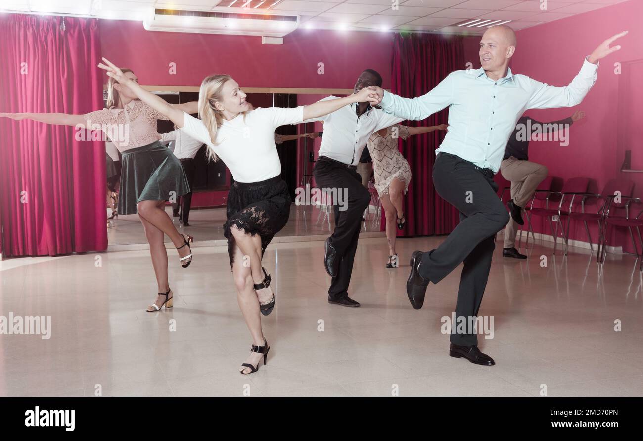 Young positive people dancing twist in pairs at dance hall together ...