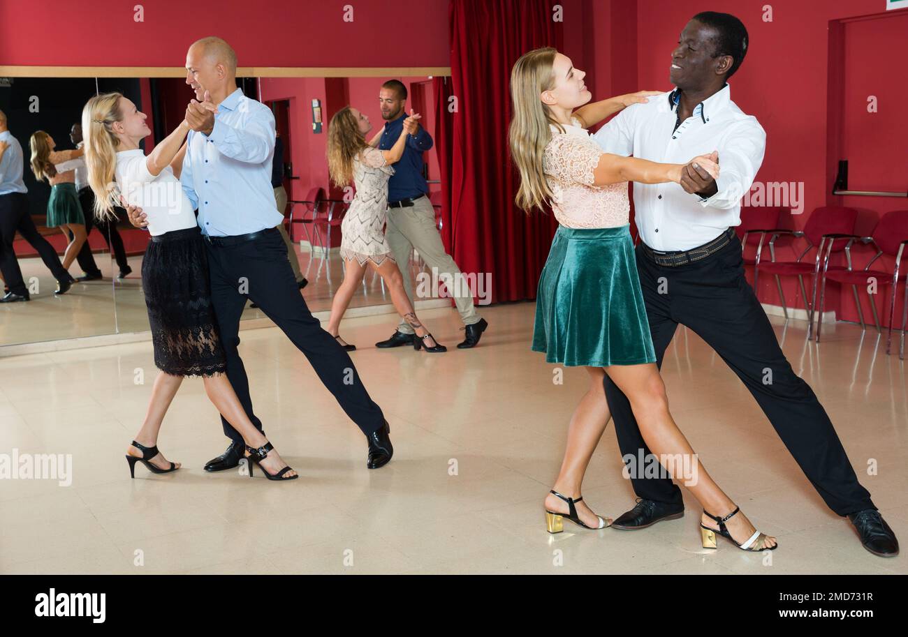 Portrait of positive adult pairs enjoying tango in modern dance hall ...