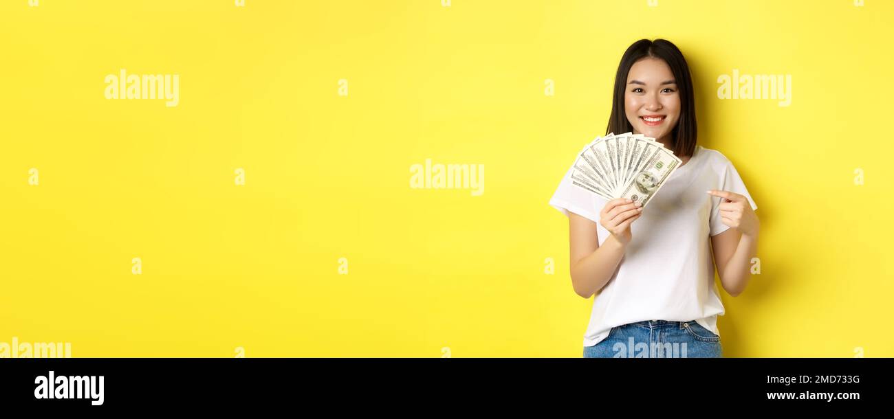 Young asian woman smiling, showing prize money, pointing finger at ...
